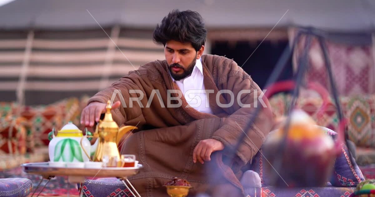 A Saudi young man pours Arabic coffee in a popular, winter morning ...