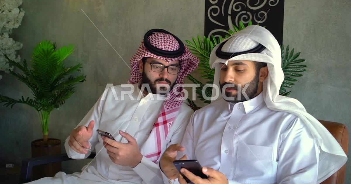 Two Saudi friends exchange information from their mobile phone inside ...