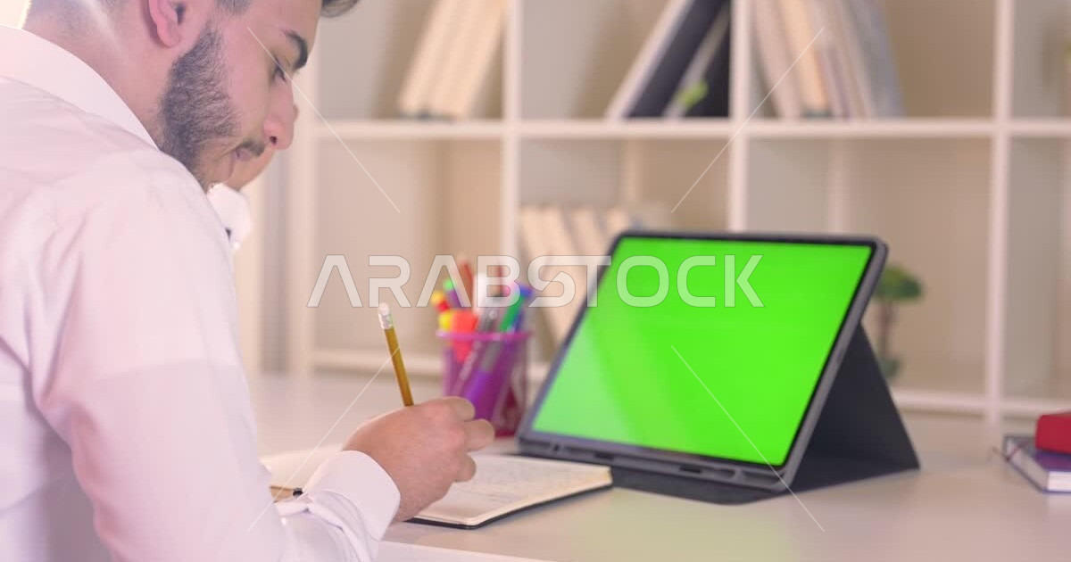 A young Saudi Arabian Gulf man studies at home using a tablet device ...