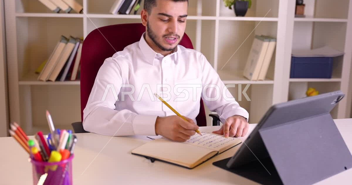 A young Saudi Arabian Gulf man studies at home using a tablet device ...