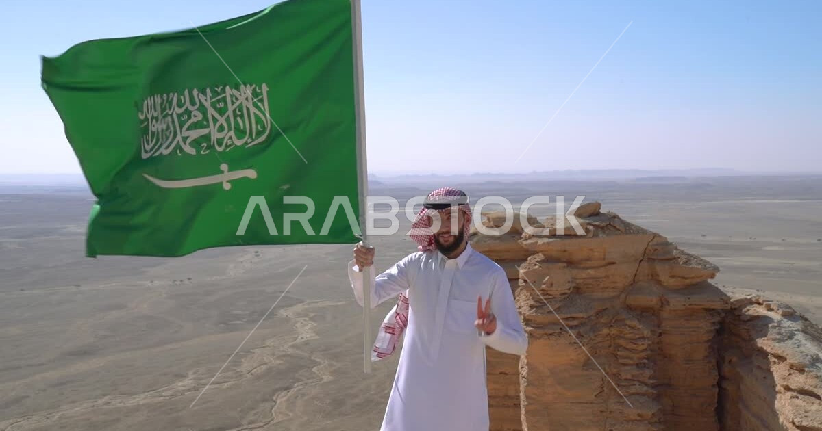 A Saudi man carrying a Saudi flag, standing in an area at the end of ...