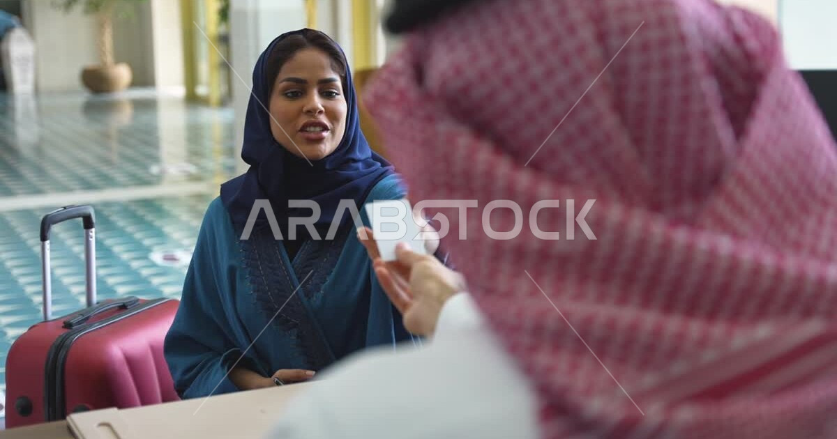 A Saudi Gulf receptionist gives a key card to a veiled Saudi female ...