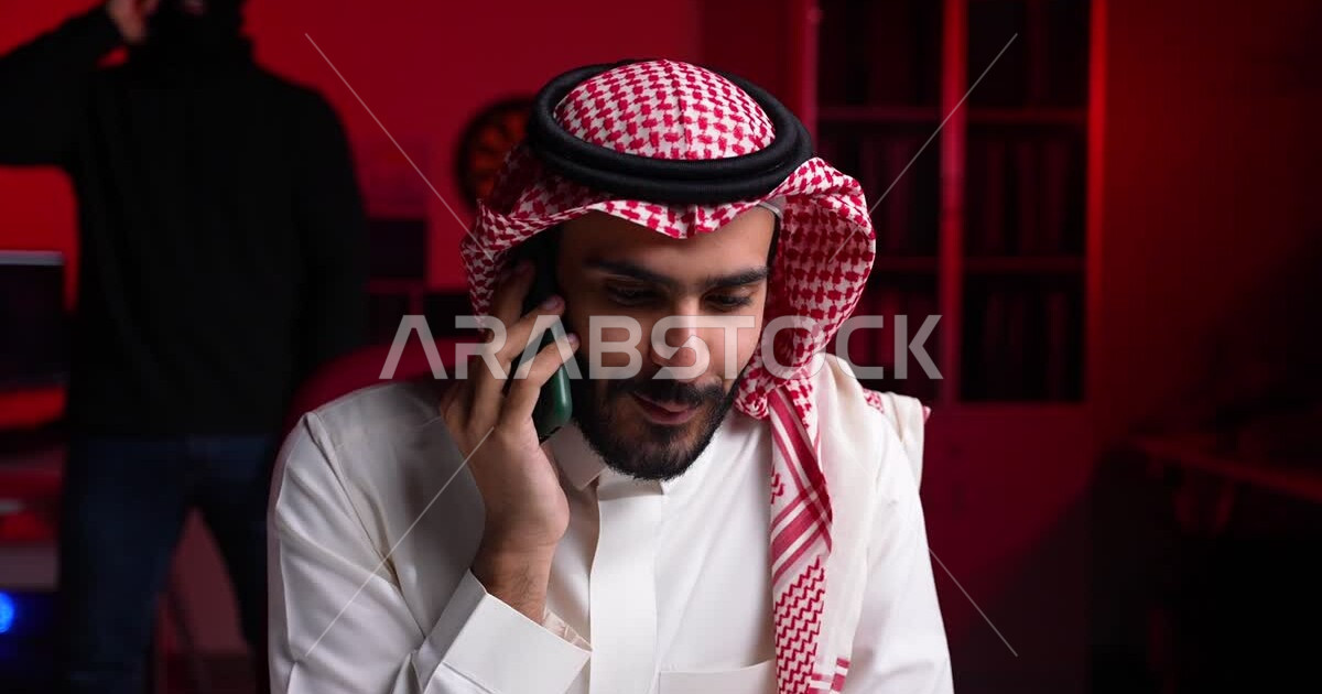 A Saudi Arabian Gulf man sitting in front of a laptop, talking on a ...
