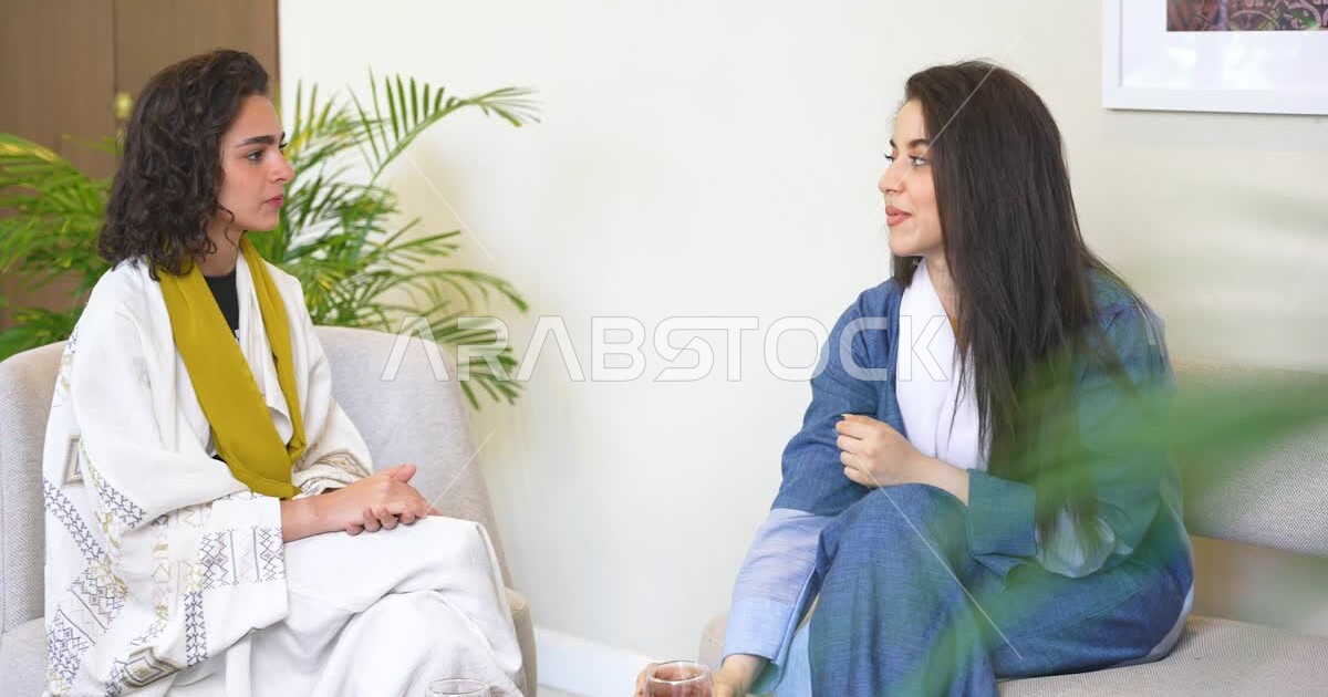 Two Saudi Arabian Gulf girls sitting together happily, talking with ...