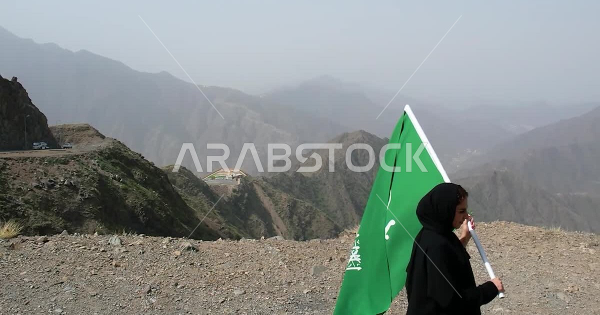 A veiled Saudi Arabian Gulf woman, holding the flag of the Kingdom of ...