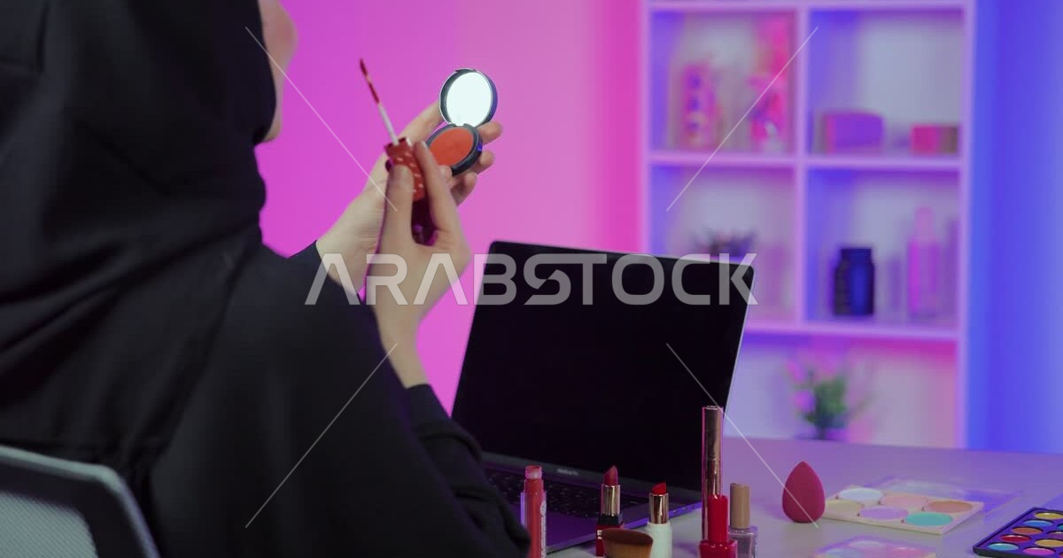 A veiled Gulf Arab Emirati makeup artist wearing a black abaya applying ...