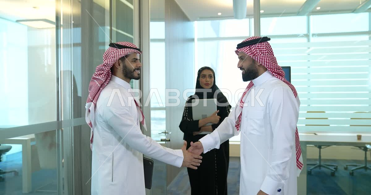 Two Saudi Arabian Gulf men shaking hands inside the company, business ...