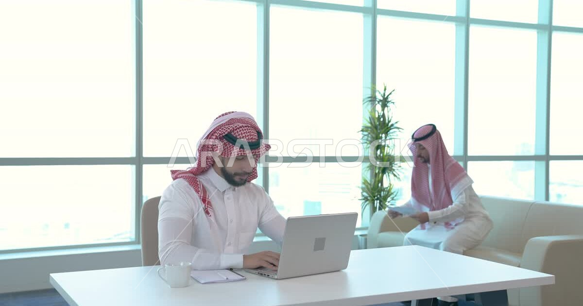 A Saudi Arabian Gulf employee using a laptop, discussing work with a ...