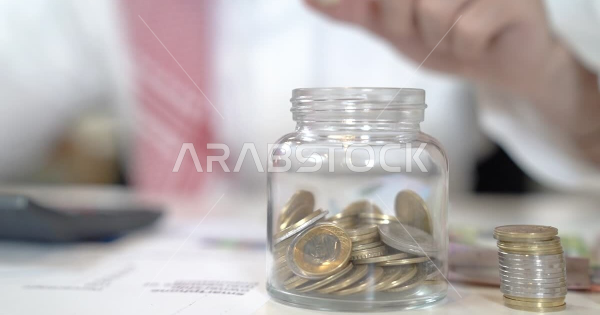 A photo shot of a Saudi Arabian Gulf man, collecting money in a glass ...
