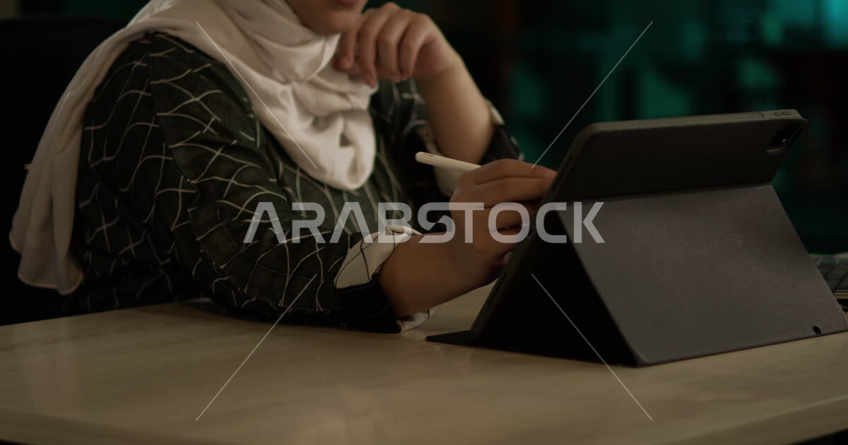 A Saudi Arabian Gulf business woman, using a tablet and a laptop to ...