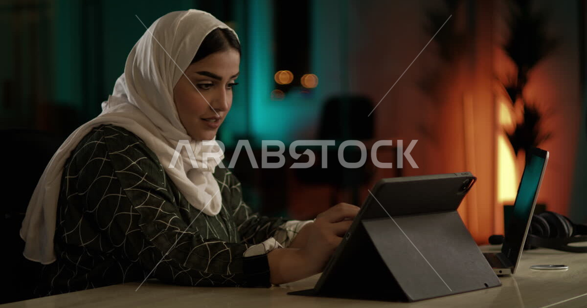 A Saudi Arabian Gulf business woman, using a tablet and a laptop to ...