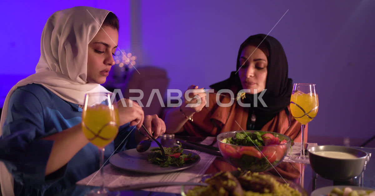 Two Arab women sitting at the dining table eating food, meeting friends ...