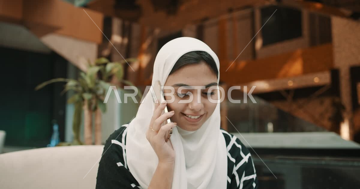 A Saudi Arabian Gulf woman makes a phone call while working on a laptop ...