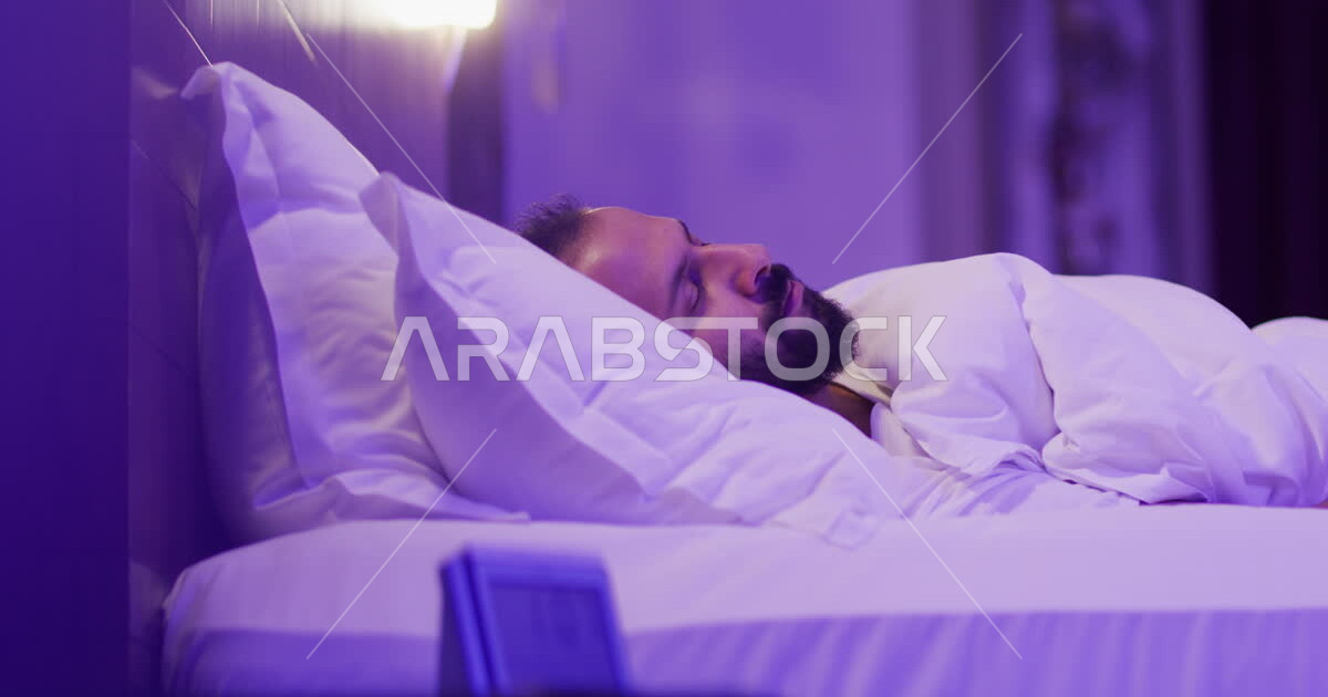 A Saudi Arabian Gulf man sleeps in a fresh and comfortable bed on a ...