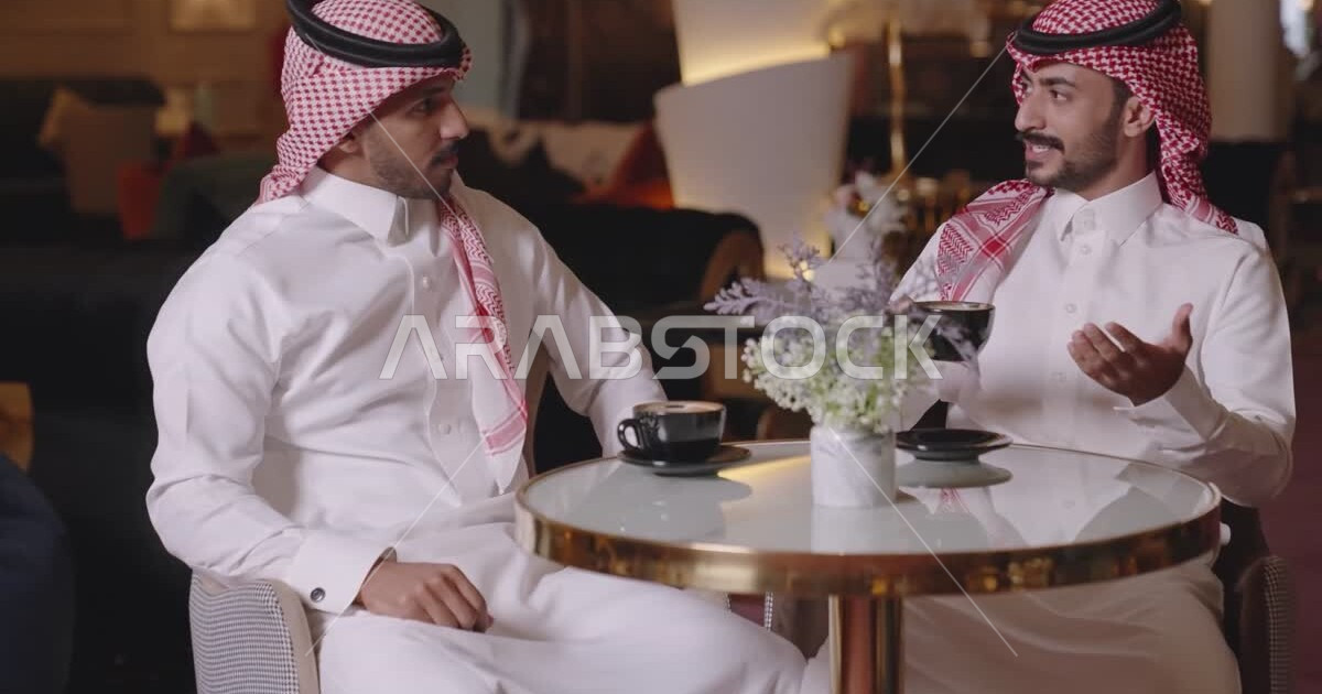 Two Saudi Arabian Gulf men are friends sitting in a café, drinking a ...