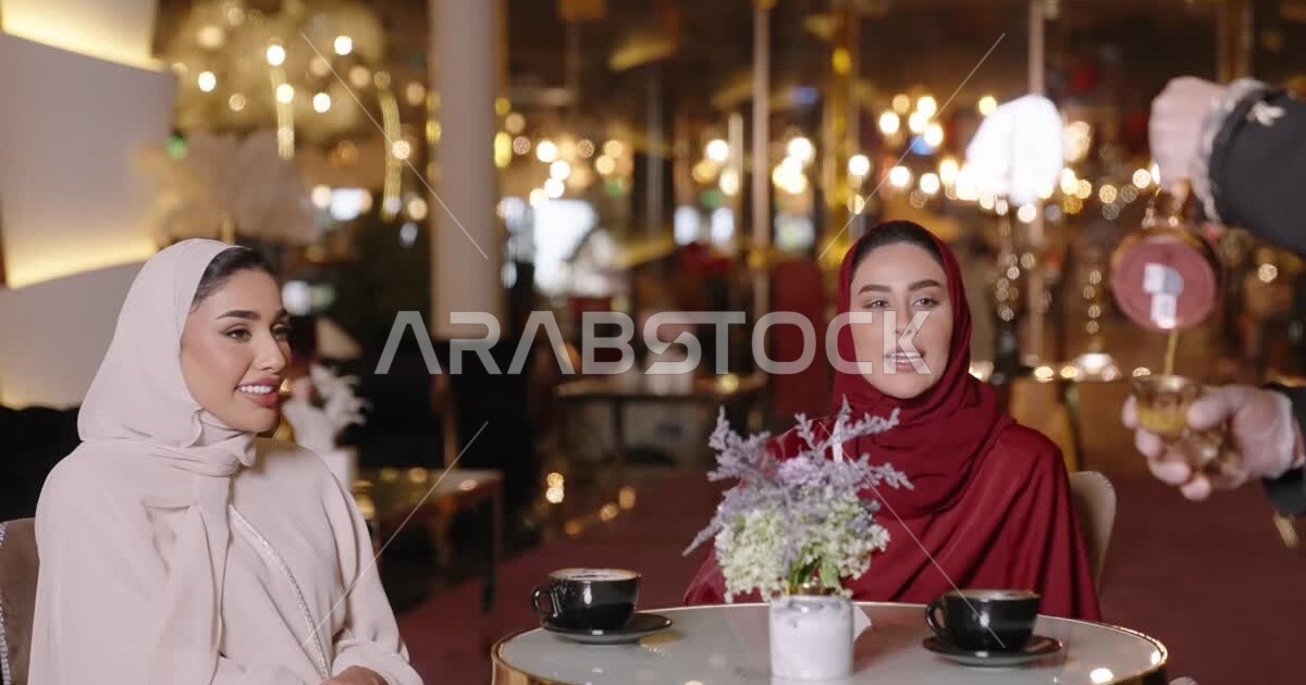 Two Saudi Arabian Gulf women sitting in a café taking a cup of hot ...