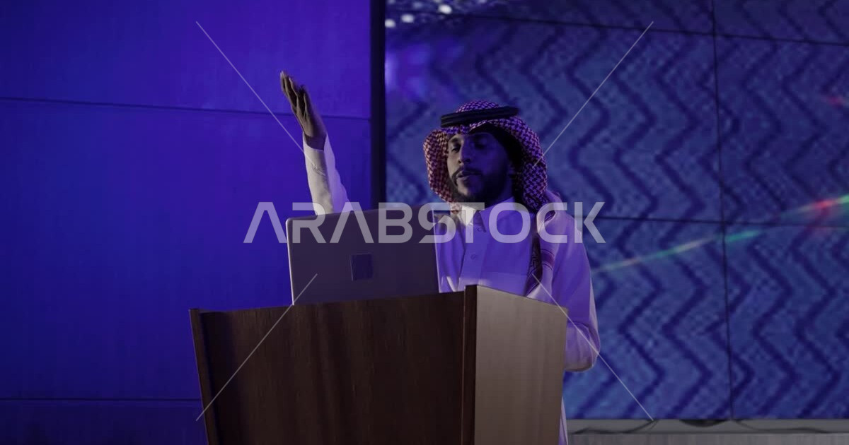 A Saudi Arabian Gulf man standing in front of a laptop, giving a ...