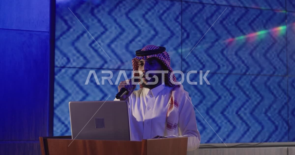A Saudi Arabian Gulf man standing in front of a laptop, giving a ...