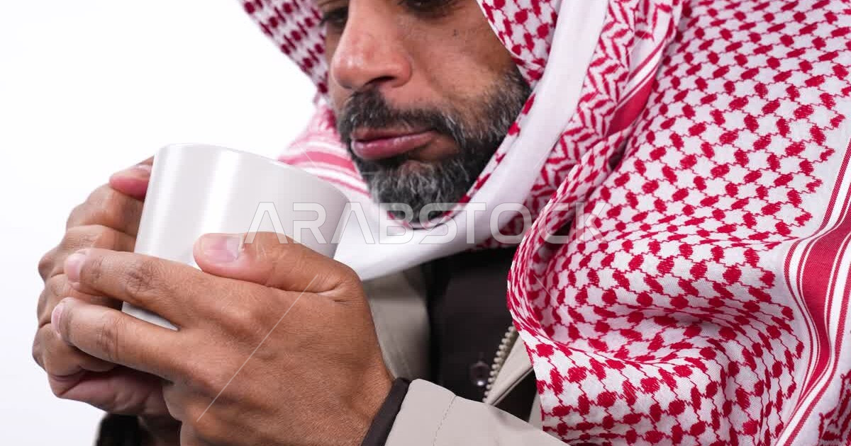Portrait of a Saudi Arabian Gulf man shivering from the cold, drinking ...