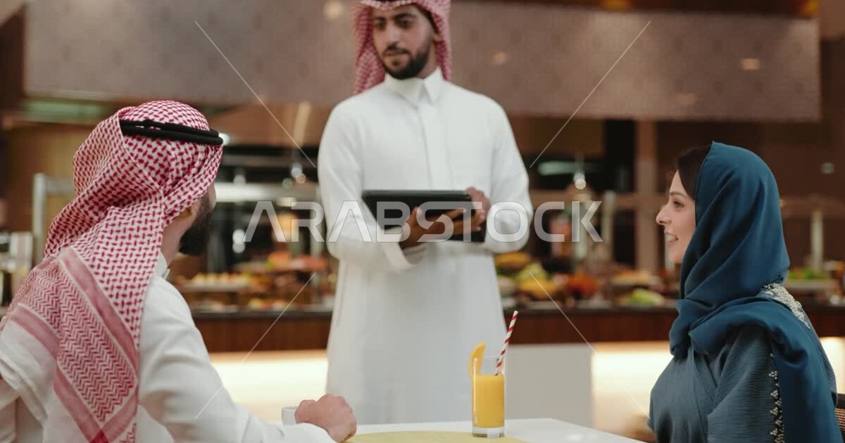 A Saudi Arabian Gulf couple sitting in a restaurant, ordering food from ...
