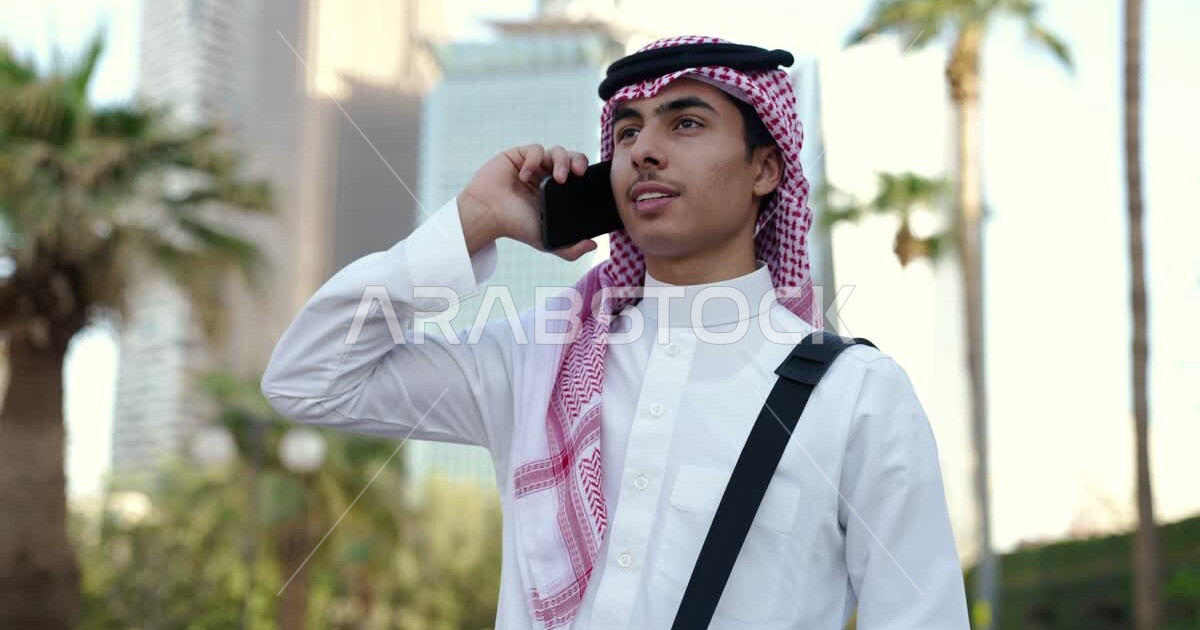 A smiling Saudi Arabian Gulf youth with a mobile phone making a phone ...