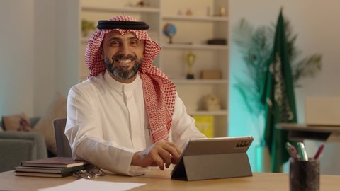 A portrait of a Saudi man wearing traditional attire sitting on a ...