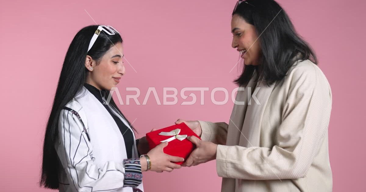 Portrait of a Saudi Arabian Gulf mother gifting her daughter a red gift ...