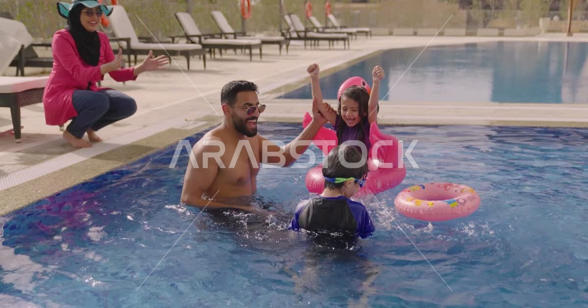 A Saudi Arabian Gulf family enjoying swimming in the water pool, a ...