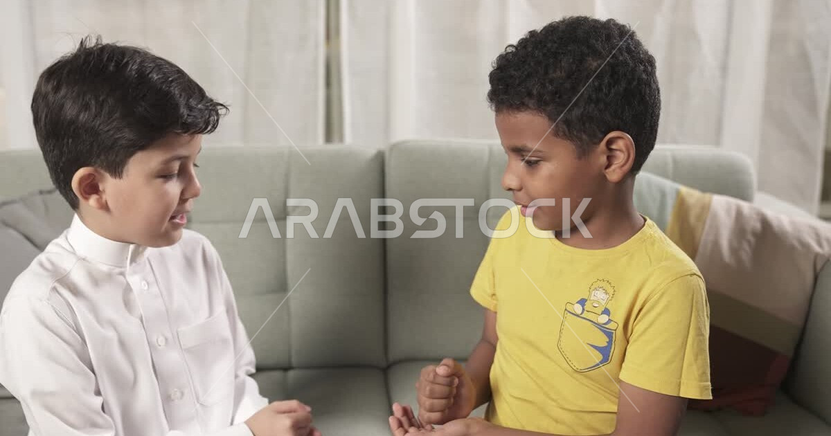 Two happy Saudi Arabian Gulf children enjoying playing the game room ...