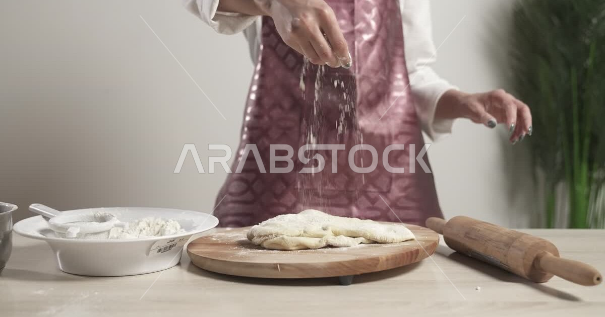 A Saudi Arabian Gulf woman, standing in front of a table with ...