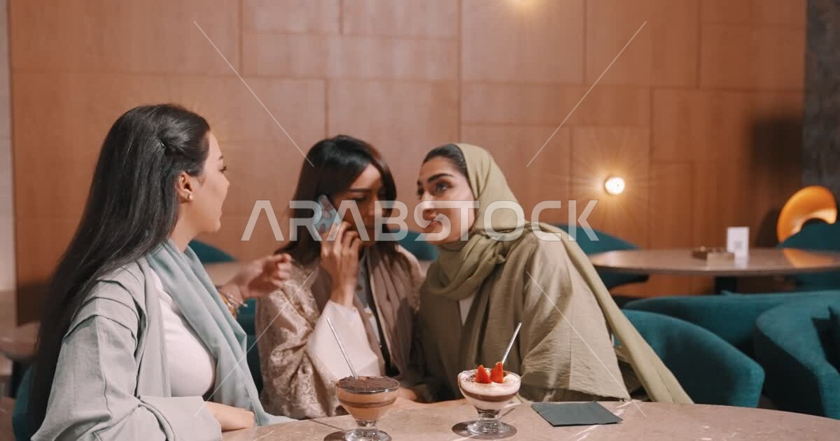 Saudi Gulf Arab female friends sitting in a café, making a phone call ...