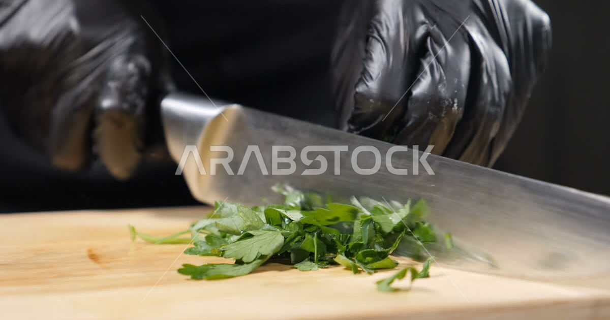 Close-up photography of a chef's hand cutting green herb, chopping ...