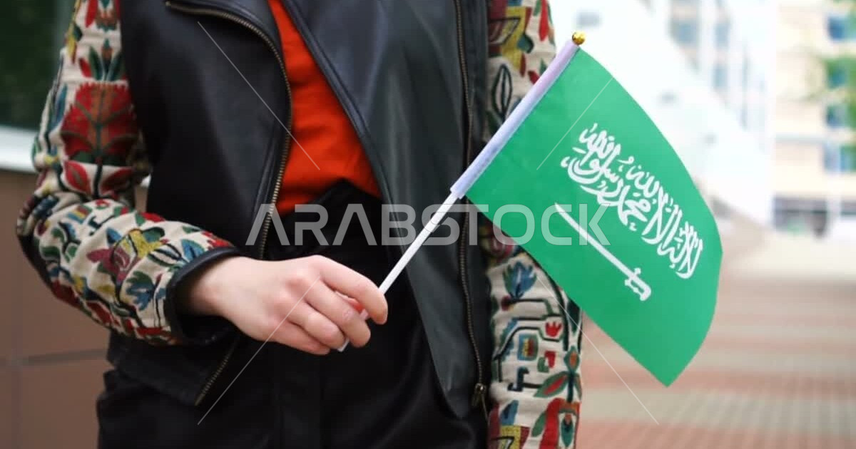Close-up of a woman holding the flag of the Kingdom of Saudi Arabia ...