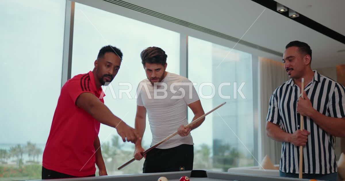 A group of Saudi Arabian Gulf friends playing billiards, recreational ...