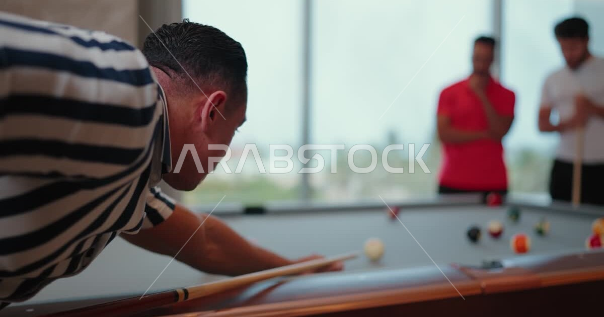 A group of Saudi Arabian Gulf friends playing billiards, recreational ...