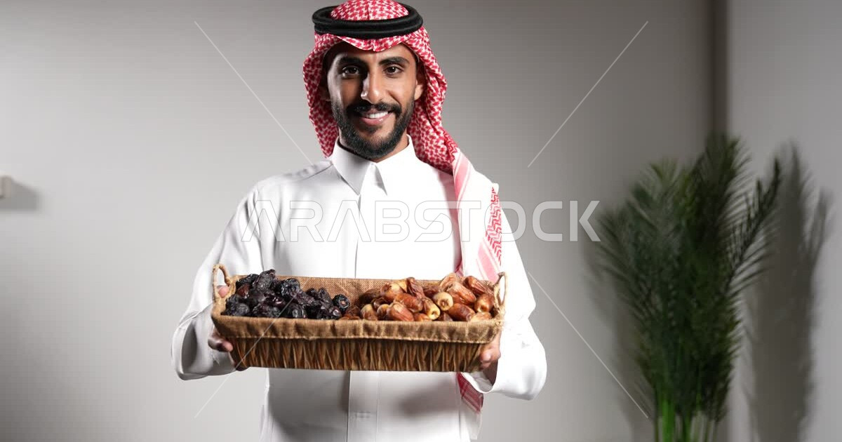 A Saudi Arabian Gulf man wearing traditional Saudi dress holds a straw ...