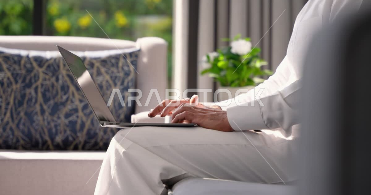 A Saudi Arabian Gulf man sitting at home, using a laptop, browsing the ...
