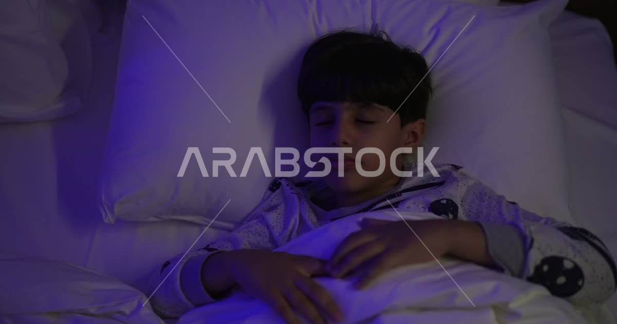 A close-up of a Saudi Arabian Gulf child sleeping on the bed, bedtime ...