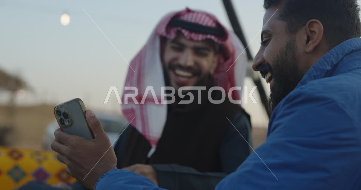Two Saudi Arabian Gulf men dressed in warm winter clothes and browsing ...