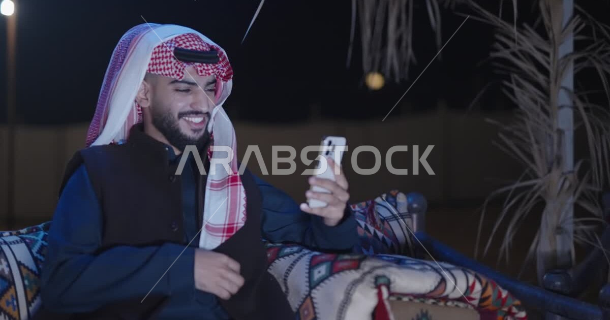 A Saudi Gulf Arab man wearing warm winter clothes and using a mobile ...