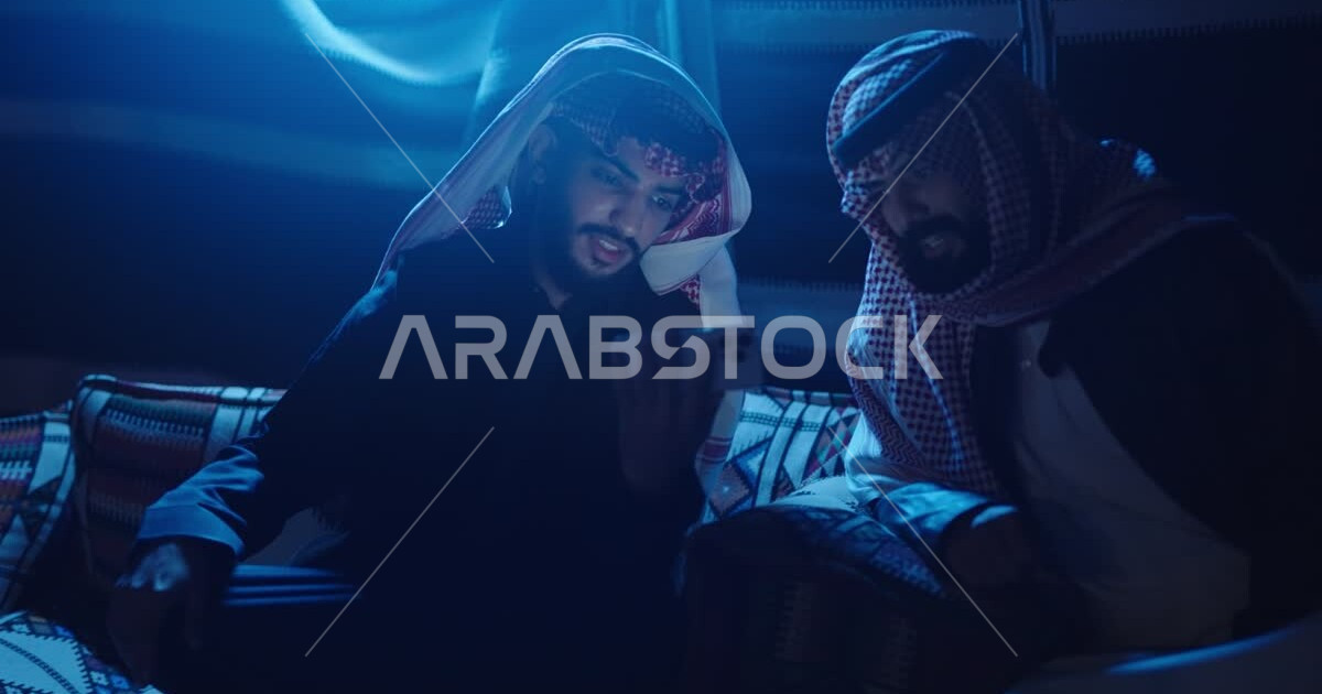 Two Saudi Arabian Gulf men dressed in warm winter clothes, using a ...