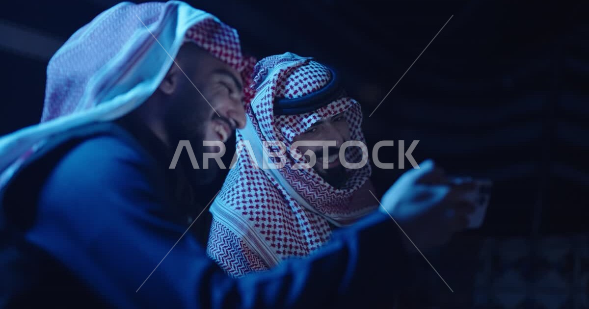 Two Saudi Arabian Gulf men dressed in warm winter clothes, using a ...
