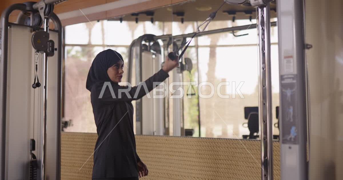 A Saudi Gulf Arab woman in the gym, wearing sports clothes, exercising ...