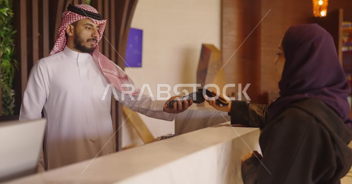 A Saudi Arab Gulf woman pays at reception electronically using a mobile ...