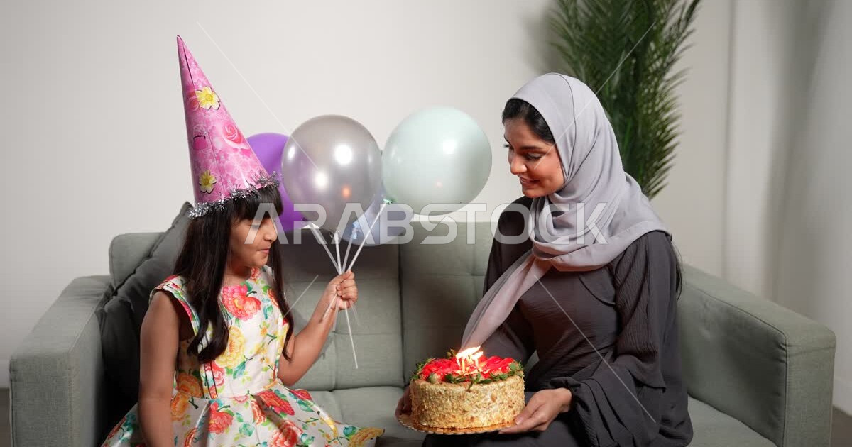 A Saudi Gulf Arab woman with her daughter sitting on the sofa, birthday ...