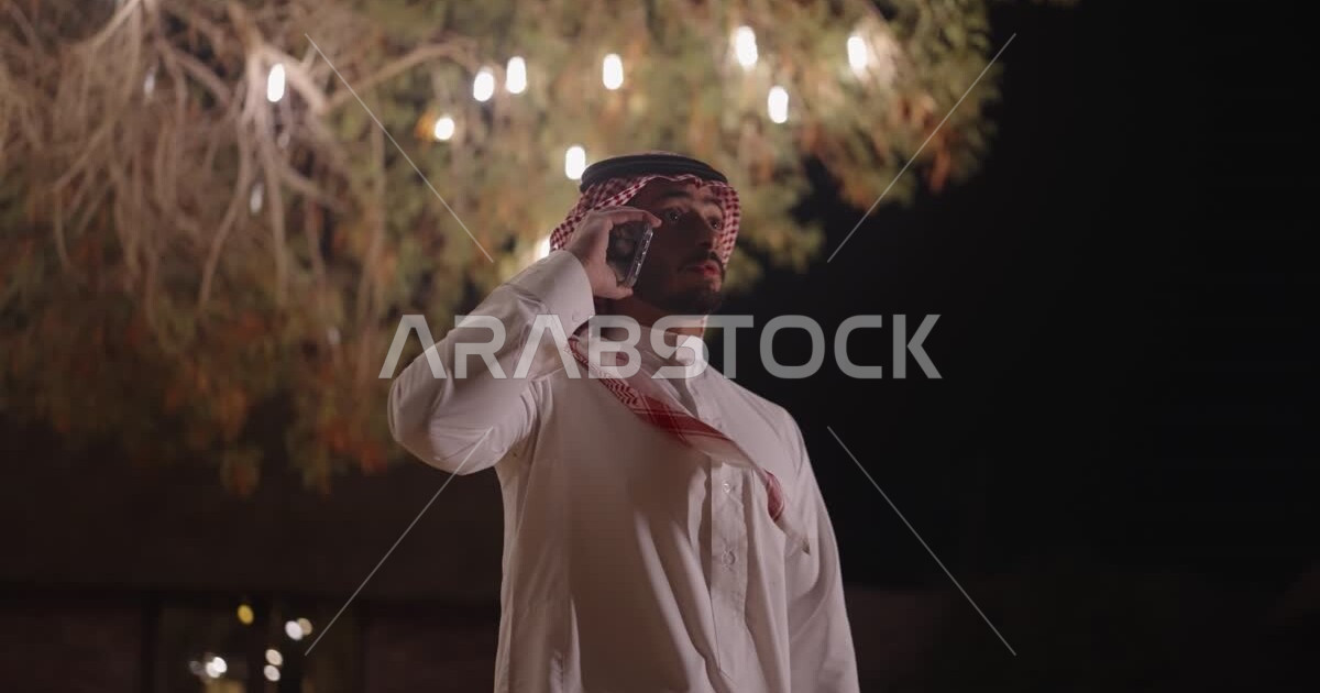 A Saudi Arabian Gulf man wearing traditional Saudi clothing uses a ...