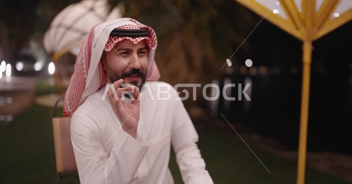 Two Saudi Arabian Gulf men sitting in a public park in the open air at ...