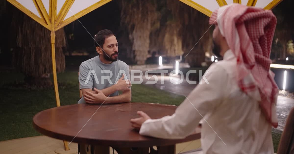 Two Saudi Arabian Gulf men sitting in a public park in the open air at ...