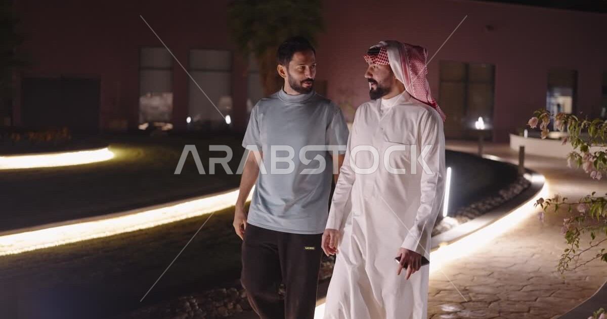 Two Saudi Arabian Gulf men walking in a public park in the open air at ...