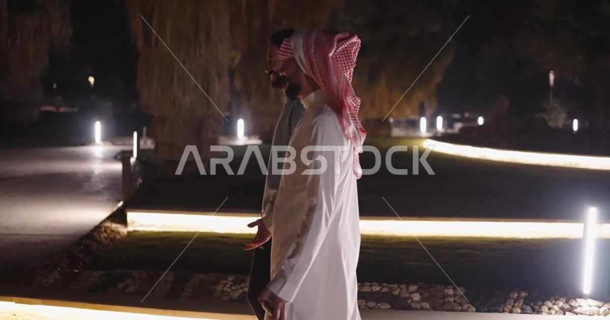 Two Saudi Arabian Gulf men walking in a public park in the open air at ...
